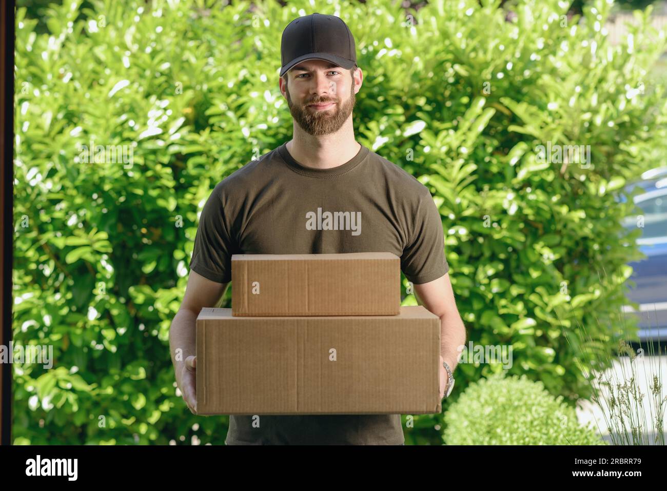 Handsome delivery man or courier with two cardboard boxes in his arms ...