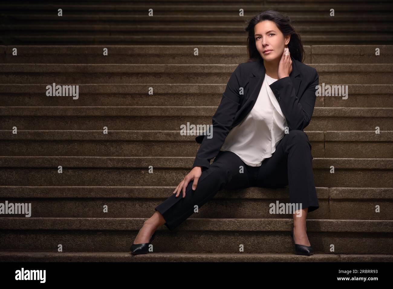 Attractive brunette woman in a slack suit sitting on urban stairs ...