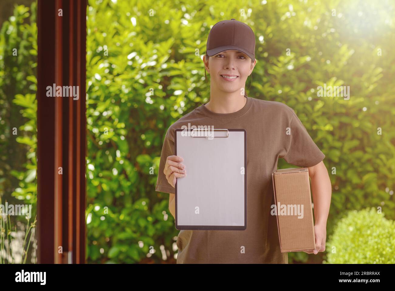 Smiling attractive female courier in a cap delivering a parcel to the ...