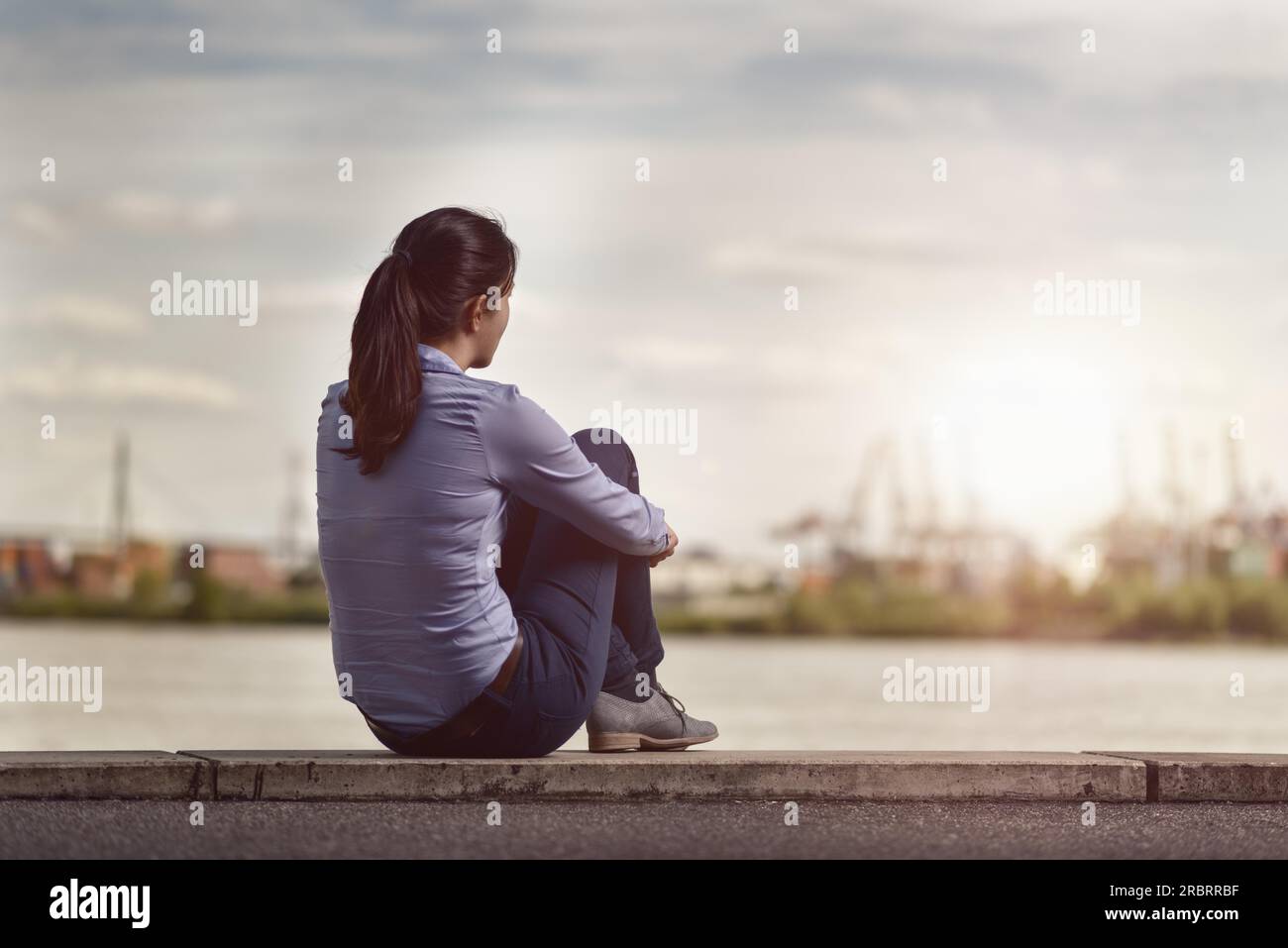 Rear View of a Thoughtful Young Woman Facing at the River while Sitting ...
