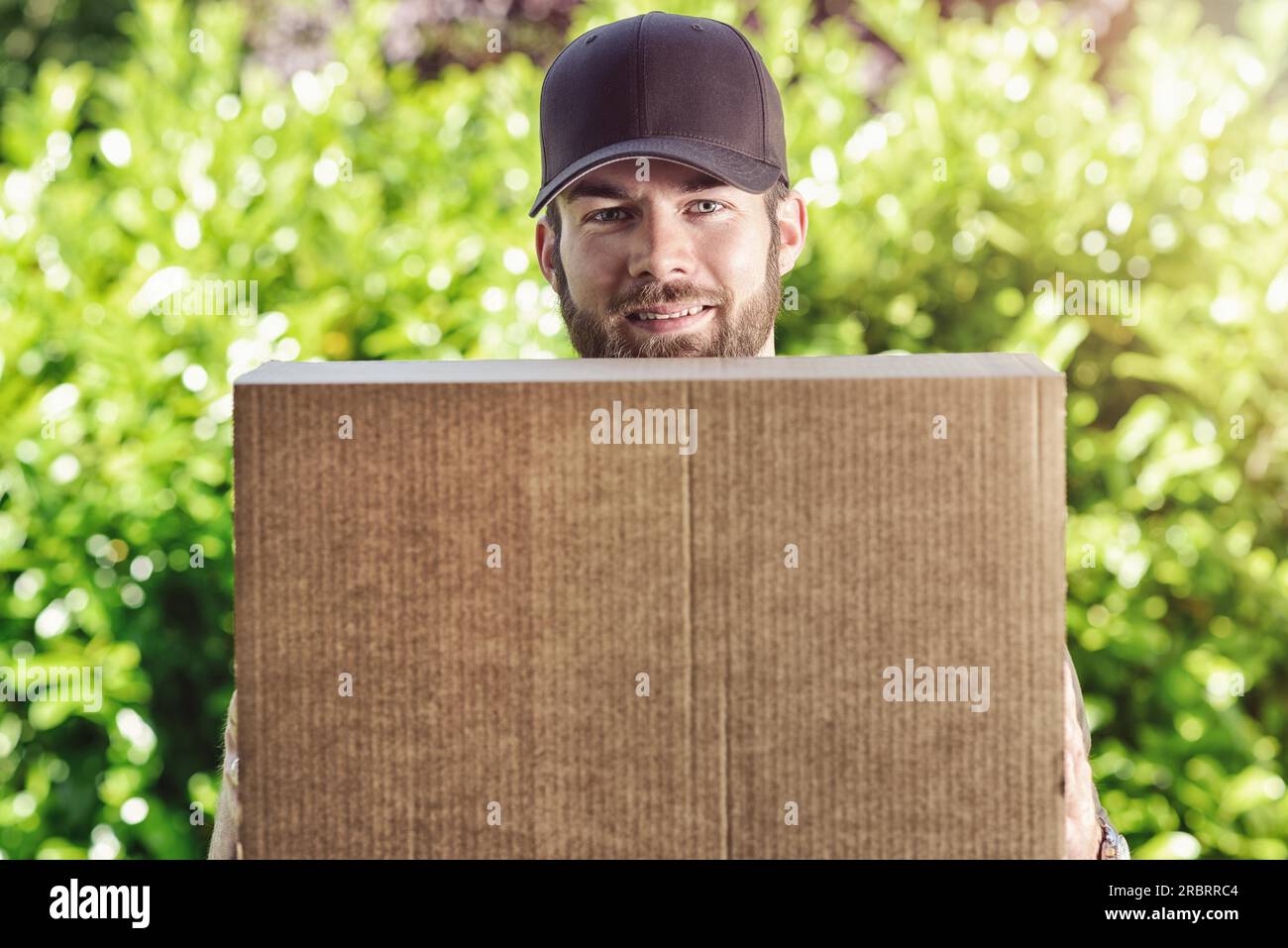Smiling postman carrying a large brown cardboard parcel waiting to make ...