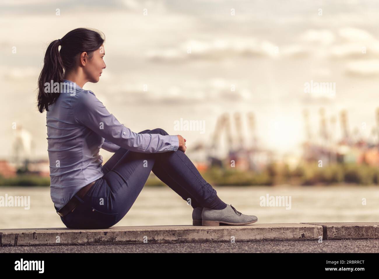 Rear View of a Thoughtful Young Woman Facing at the River while Sitting ...