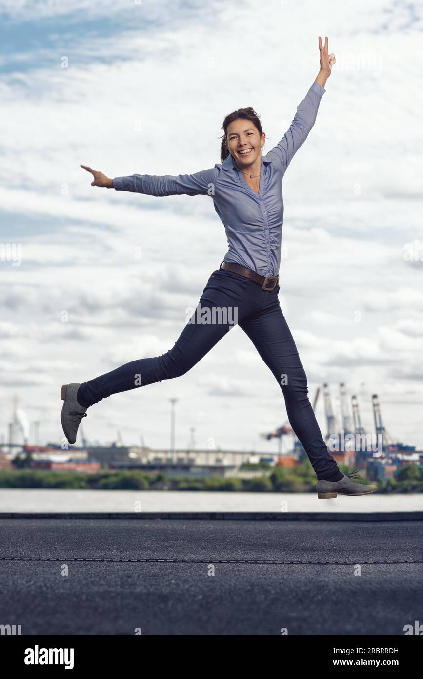 Young woman leaping and cheering for joy with her arms raised and a ...