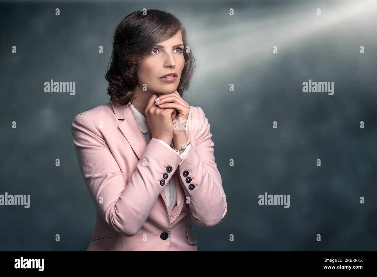 Serious young woman with her hands clasped in prayer and supplication ...