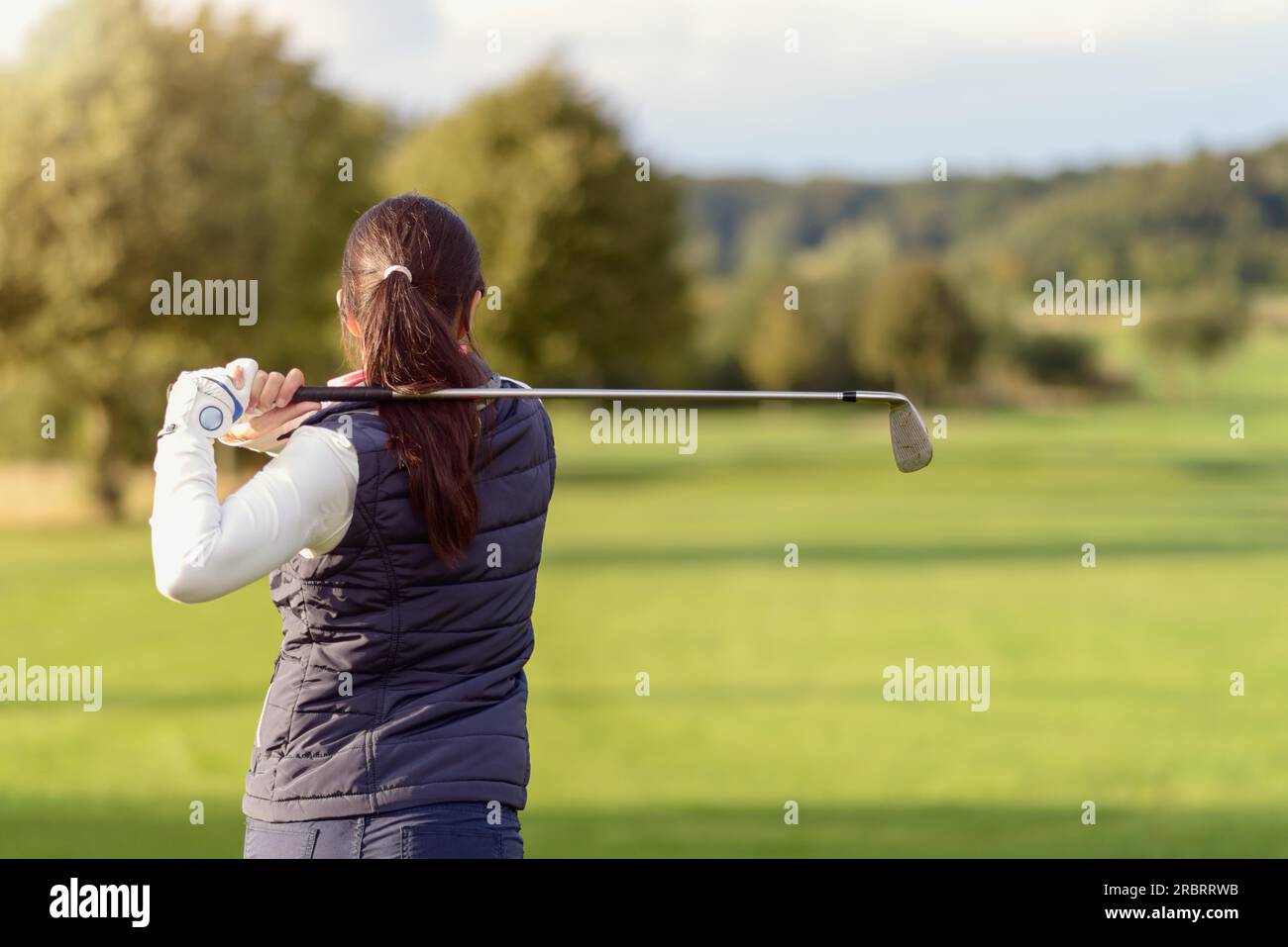 Female golfer striking a golf ball on a golf course, half body rear ...