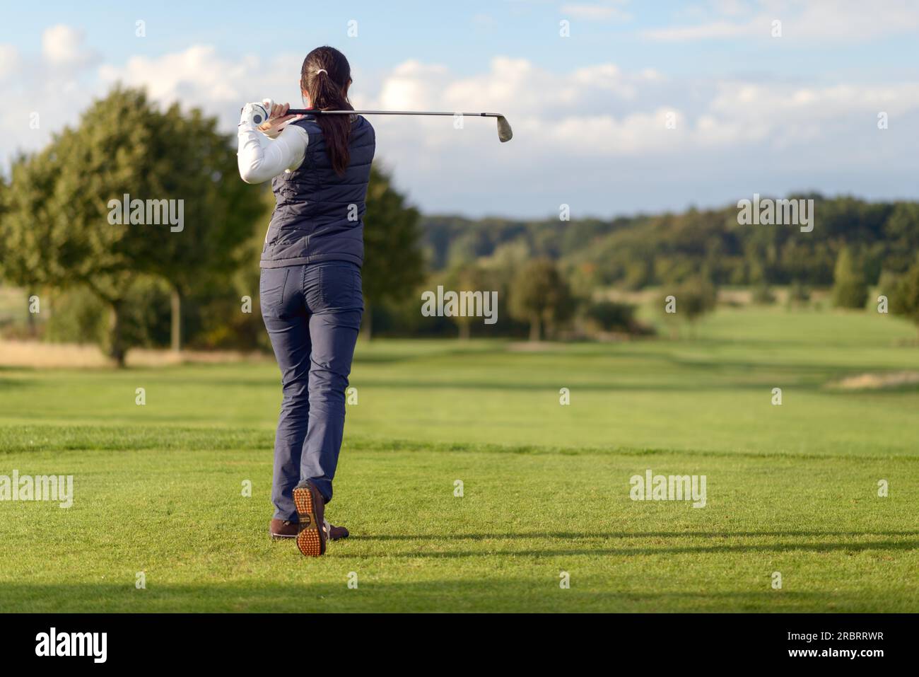 Female golfer striking a golf ball on a golf course, full body rear ...