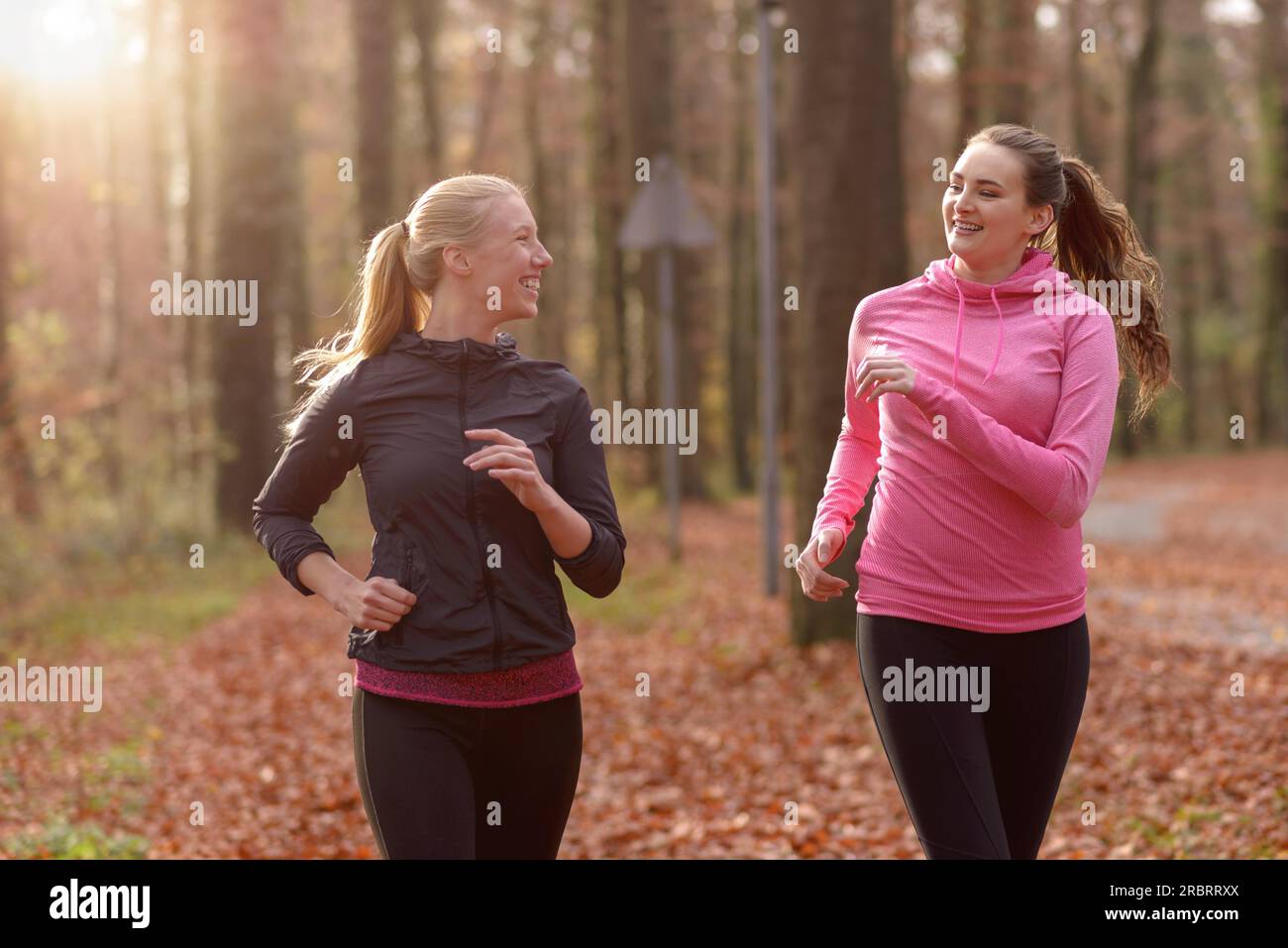 Two attractive fit young ladies out jogging together through an autumn ...