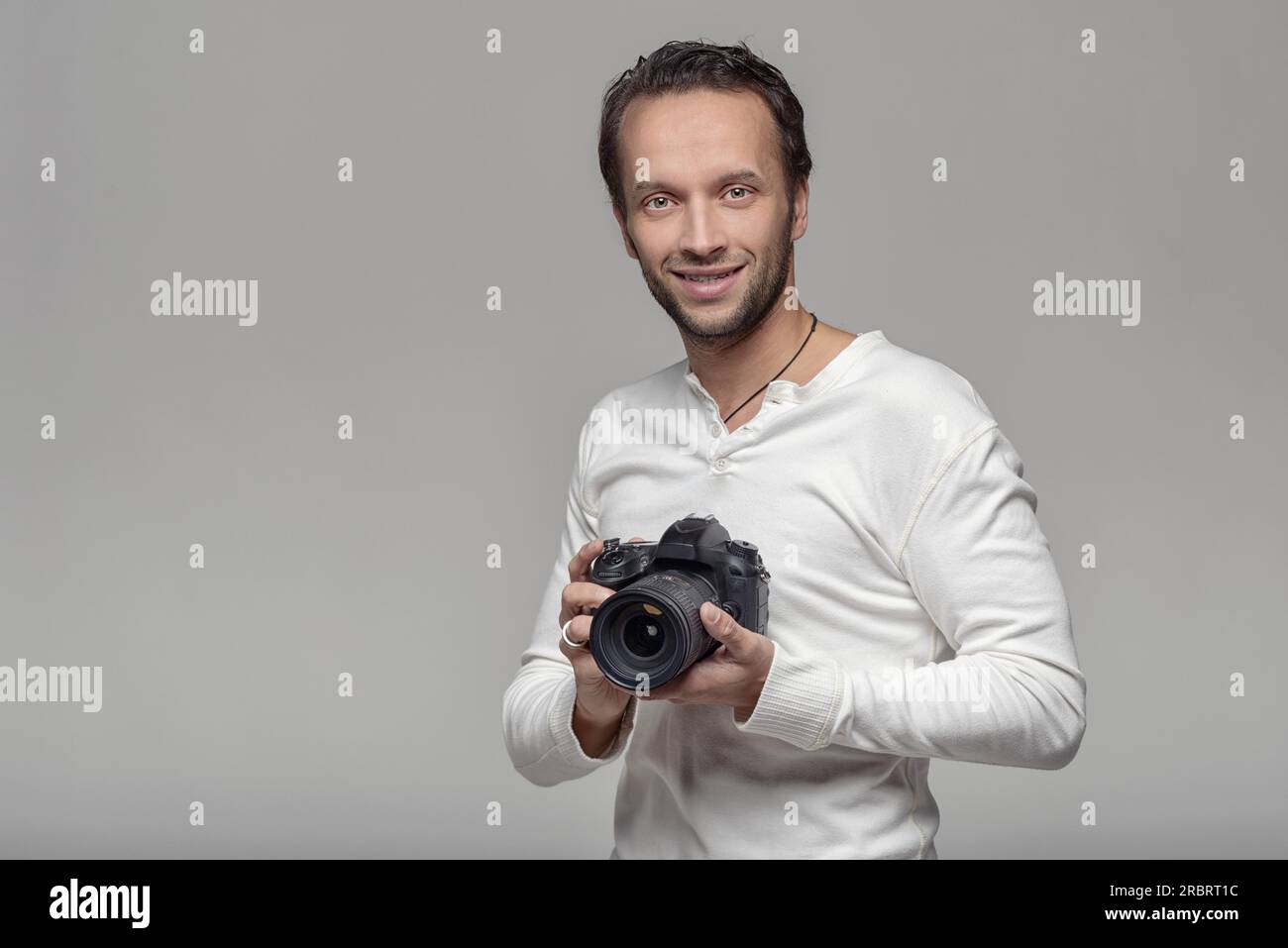 Handsome photographer with a friendly smile standing holding his camera ...