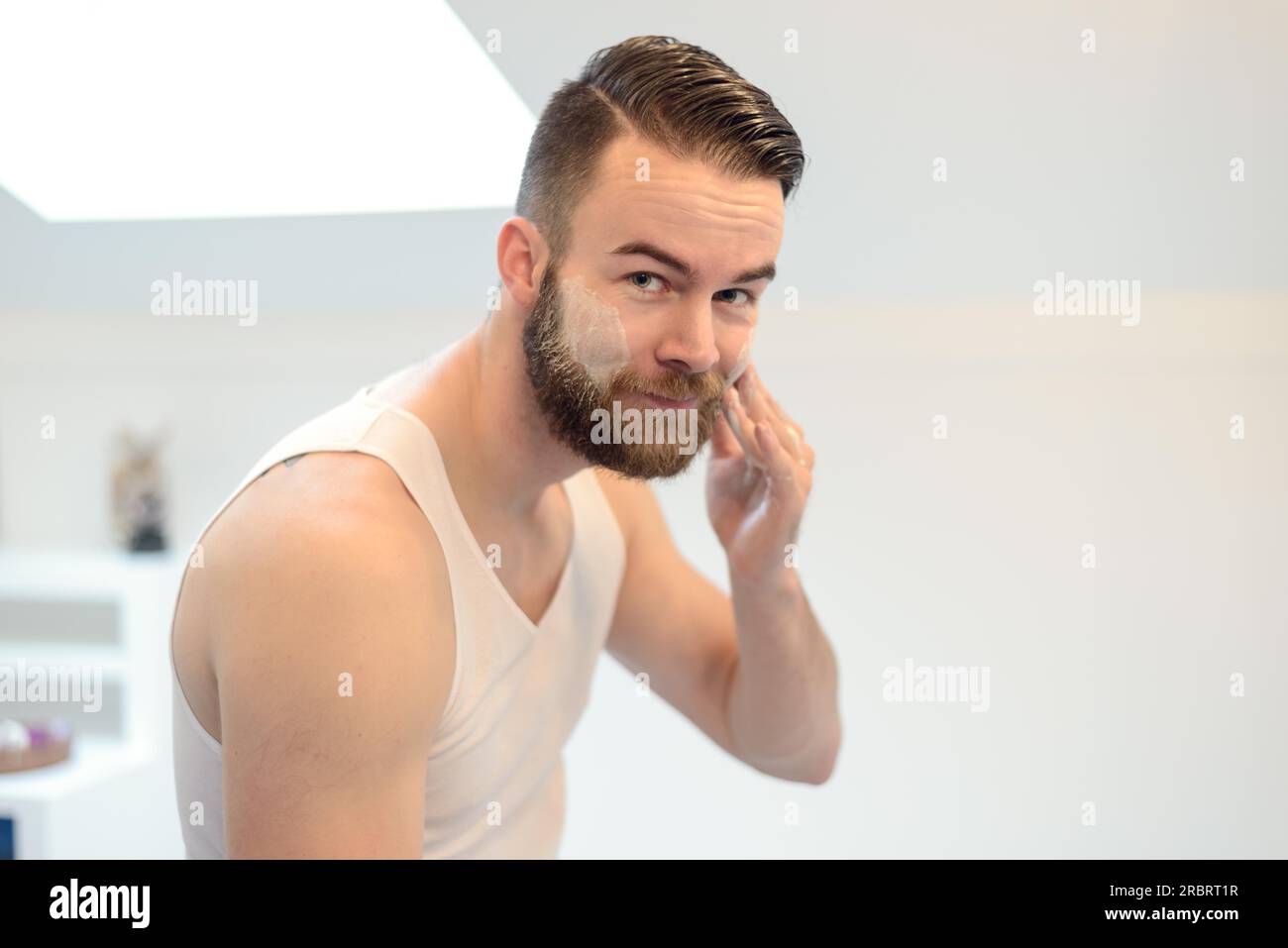 Young man applying shaving cream above his beard, morning routine, a ...