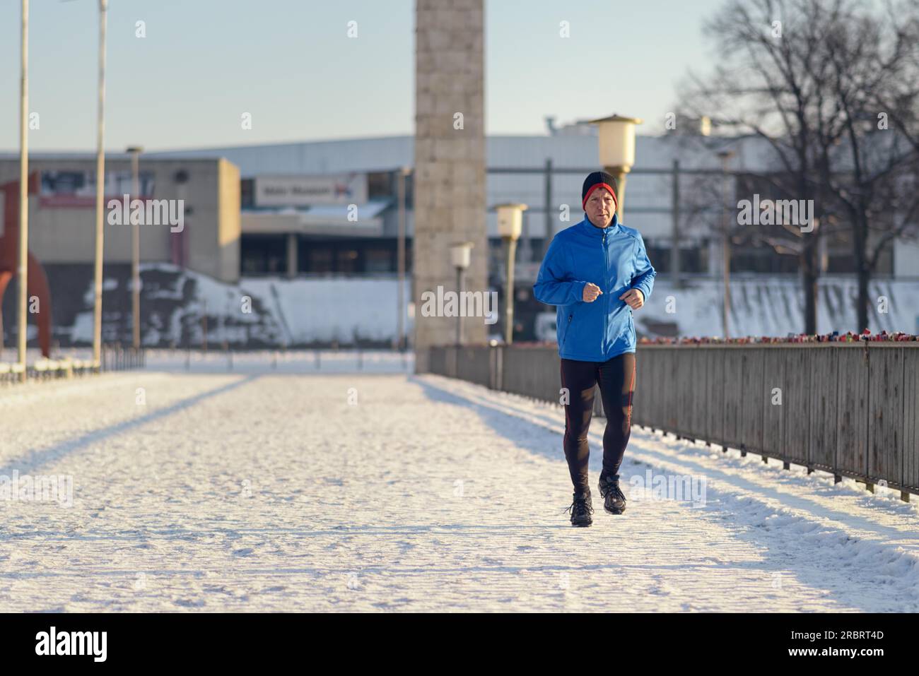 Man out in winter weather for his daily run jogging alongside a railing ...