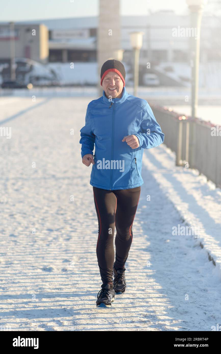 Man out in winter weather for his daily run jogging alongside a railing ...