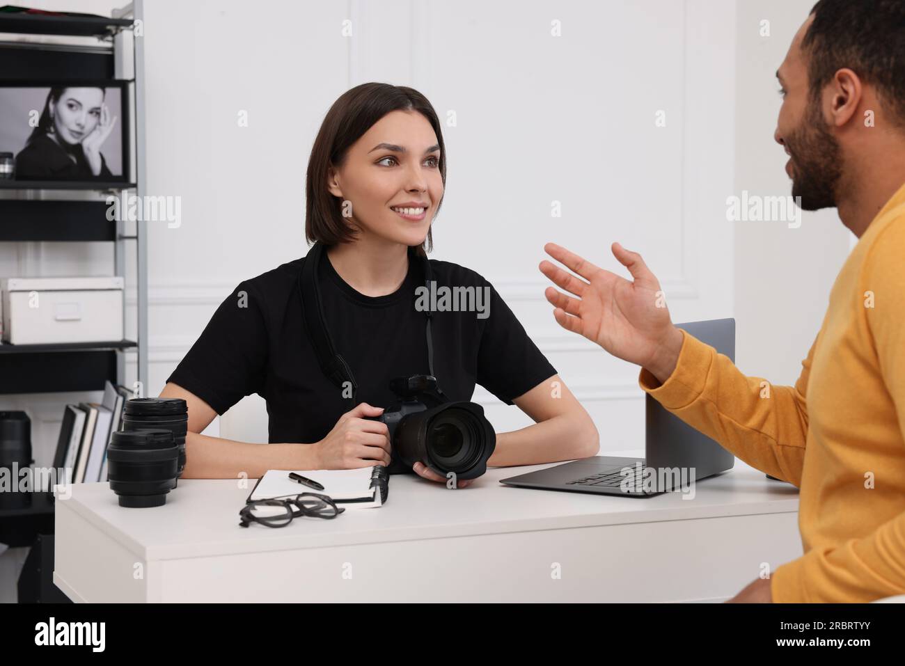 Young professional photographer holding camera while talking with man ...