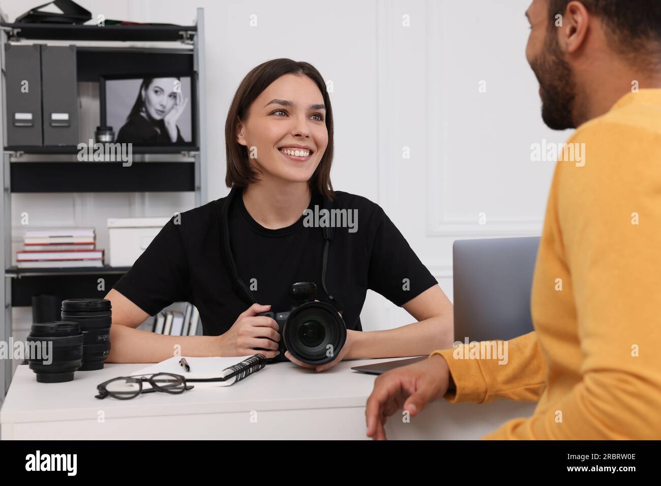 Young professional photographer holding camera while talking with man ...