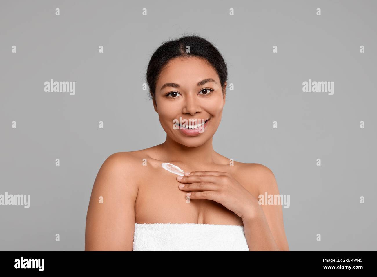 Young woman applying cream onto body on grey background Stock Photo - Alamy