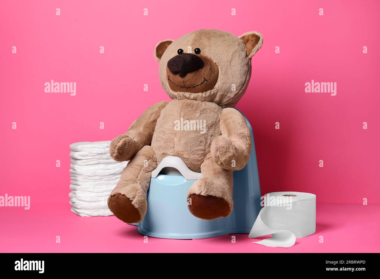 Teddy bear on baby potty, toilet paper and stack of diapers on pink ...
