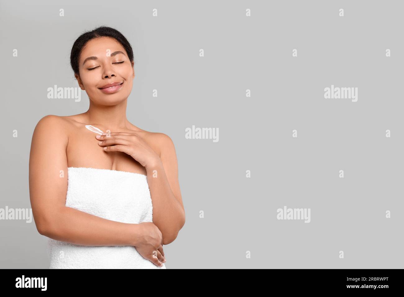 Young woman applying cream onto body on grey background. Space for text ...