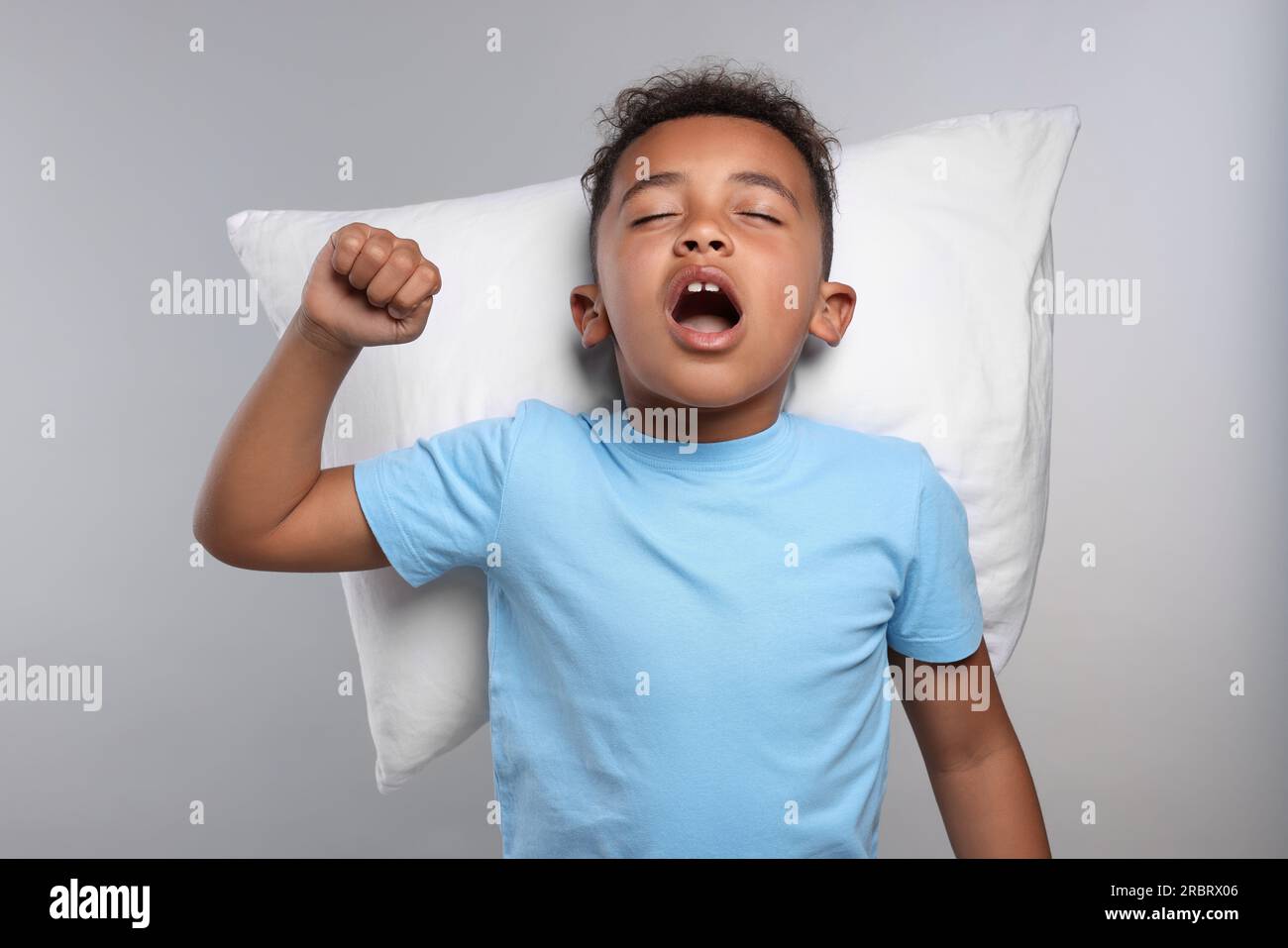 Boy with pillow yawning and stretching on grey background. Insomnia ...