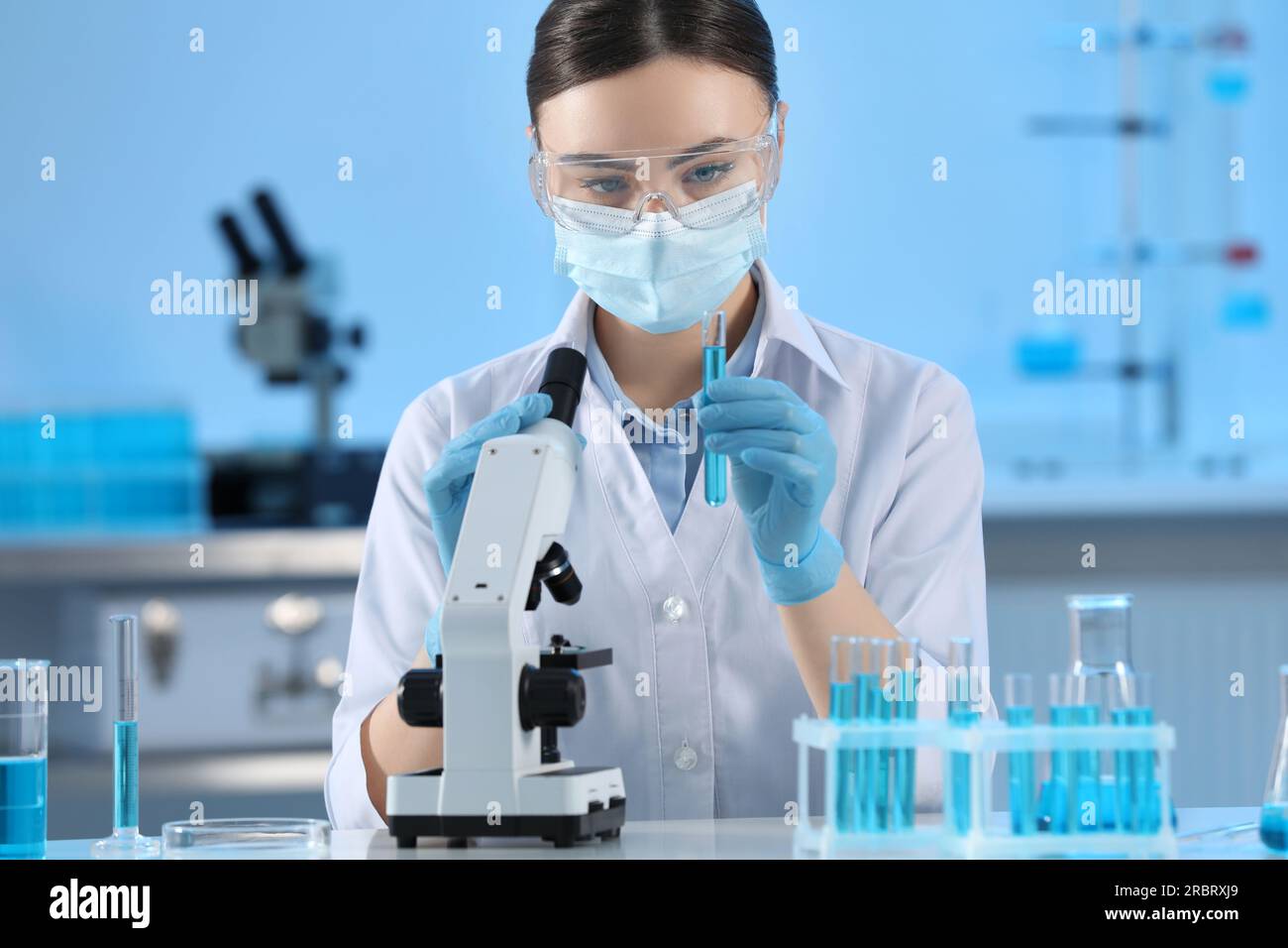 Scientist holding test tube with light blue liquid and microscope in ...