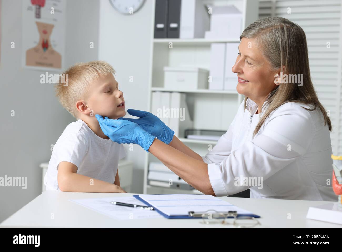 Endocrinologist examining boy's thyroid gland at table in hospital ...