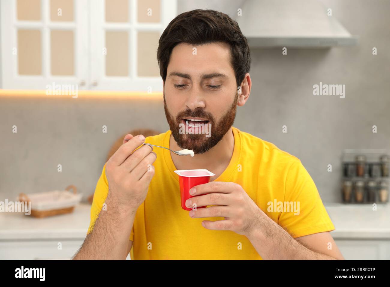 Handsome man eating delicious yogurt in kitchen Stock Photo - Alamy