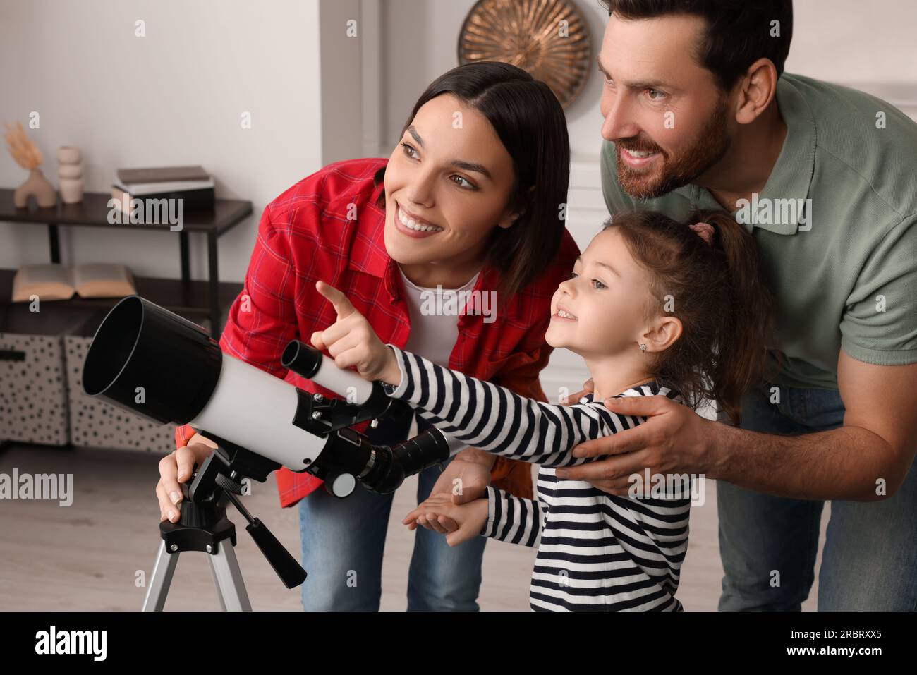 Happy family using telescope to look at stars in room Stock Photo - Alamy