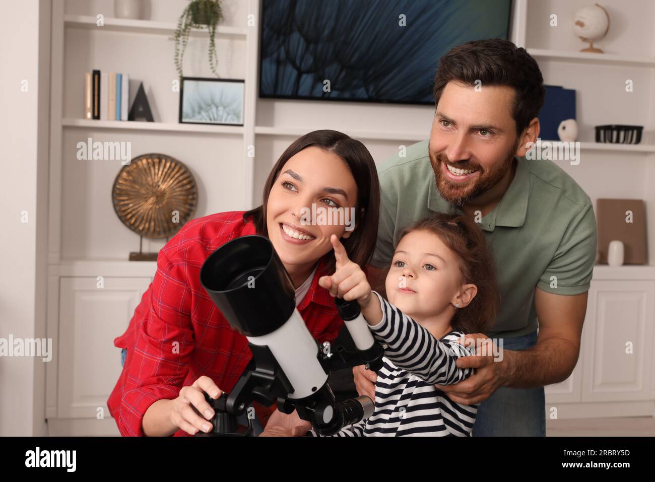 Happy family using telescope to look at stars in room Stock Photo - Alamy