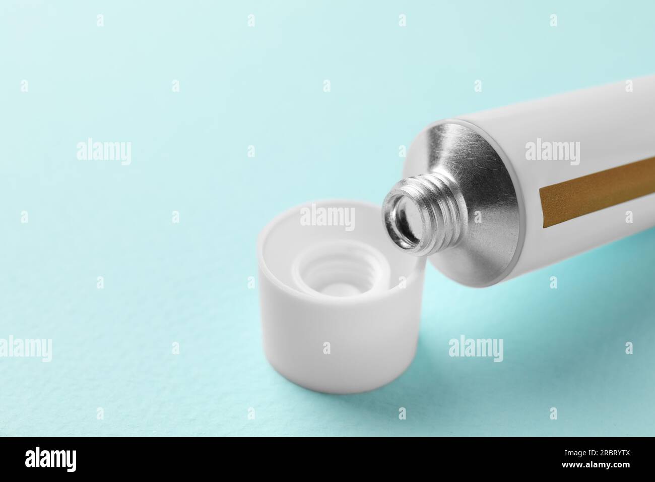 Open tube of ointment on light blue background, closeup. Space for text ...