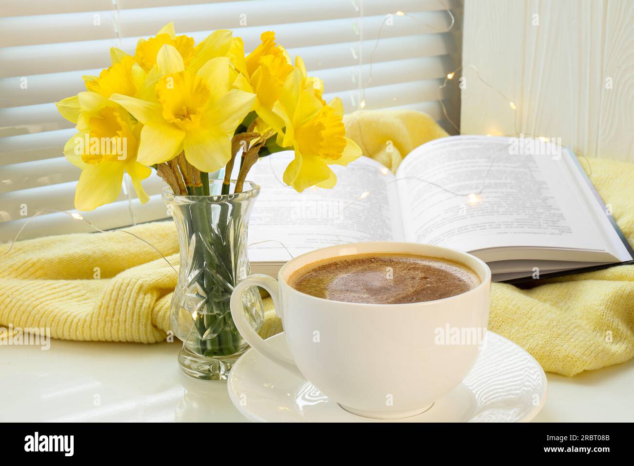 Beautiful yellow daffodils in vase, cup of coffee, book and festive ...