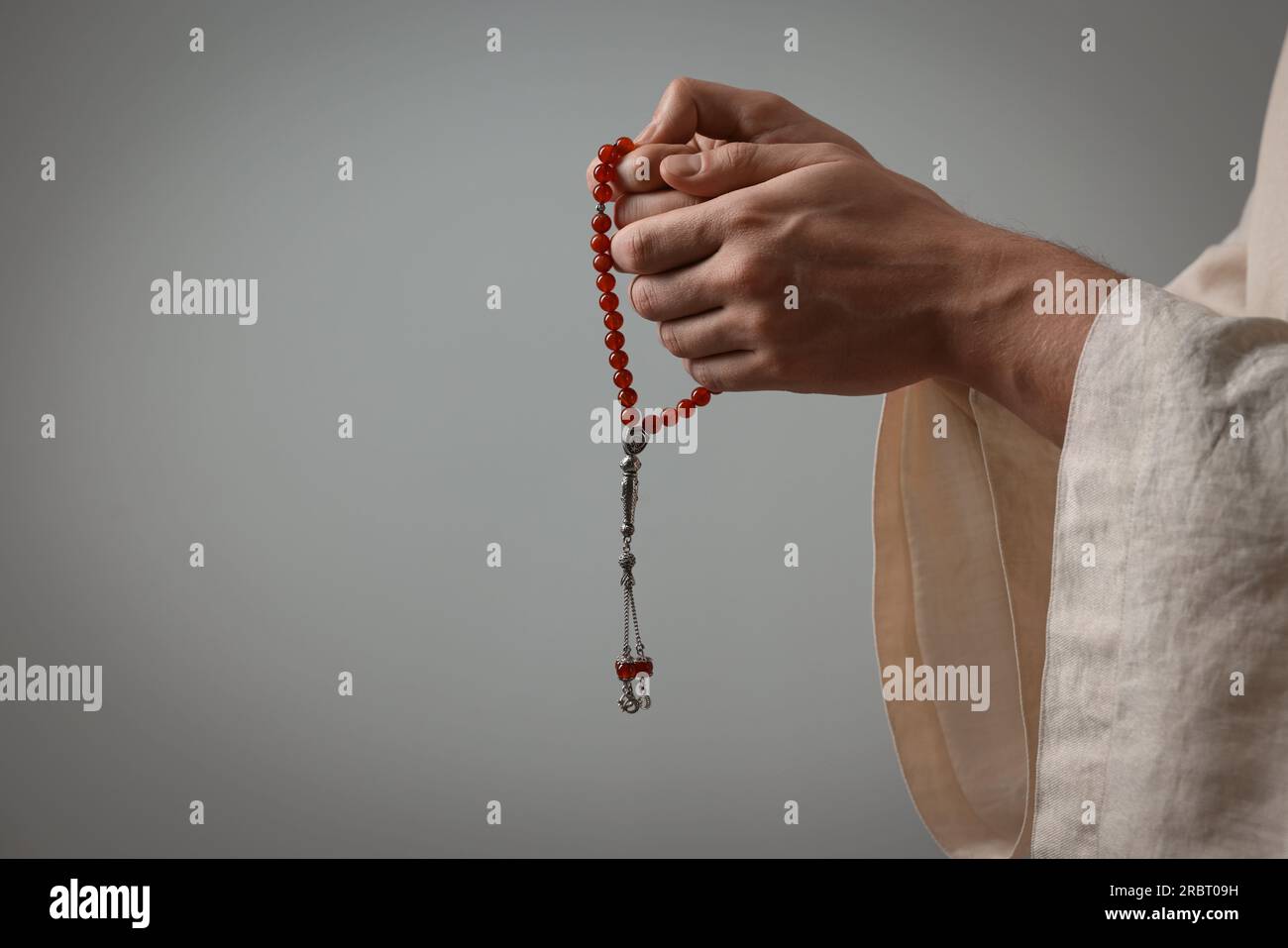 Muslim man with misbaha praying on light grey background, closeup ...