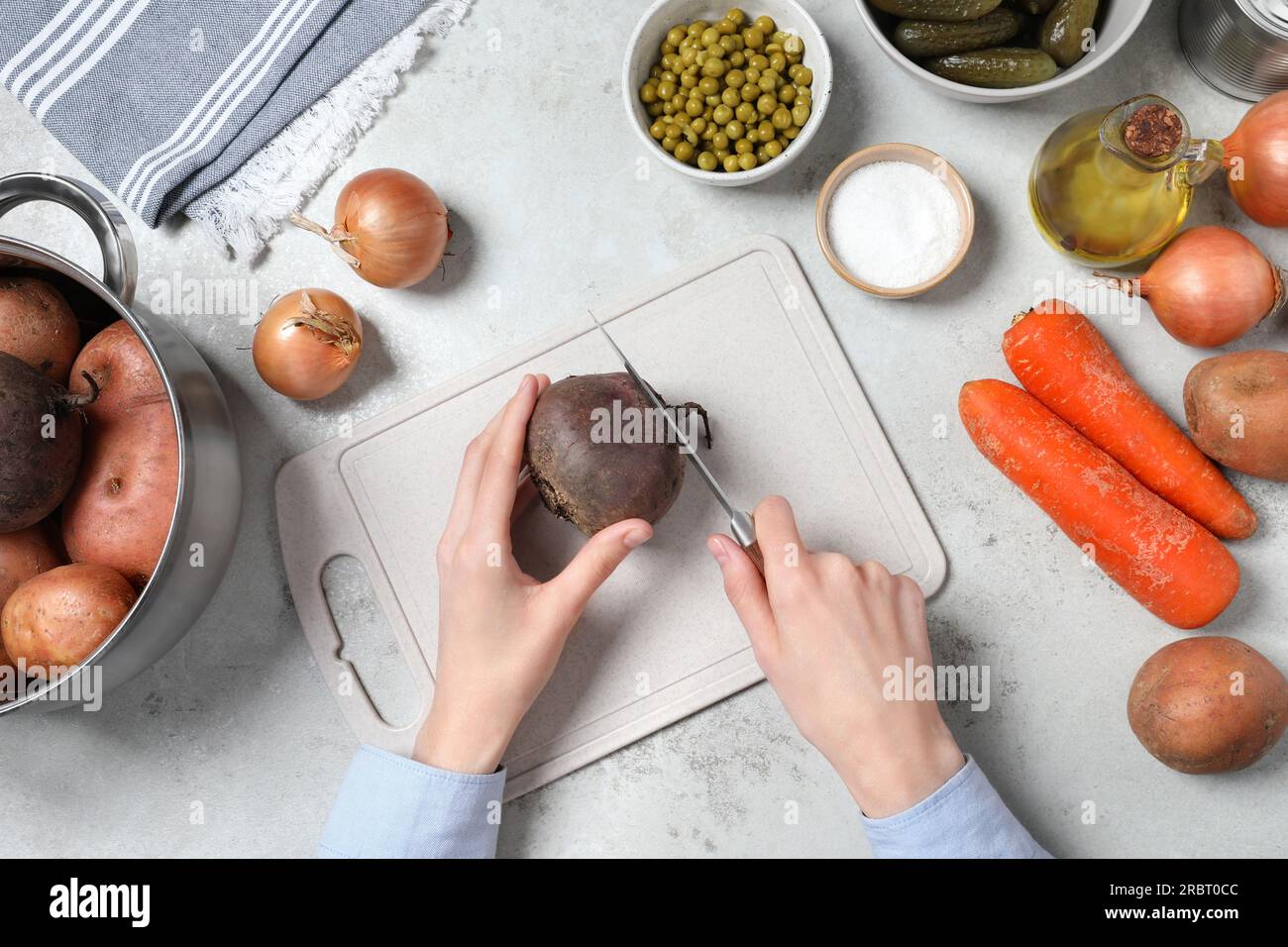 Woman peeling beetroot at white table, top view. Cooking vinaigrette ...