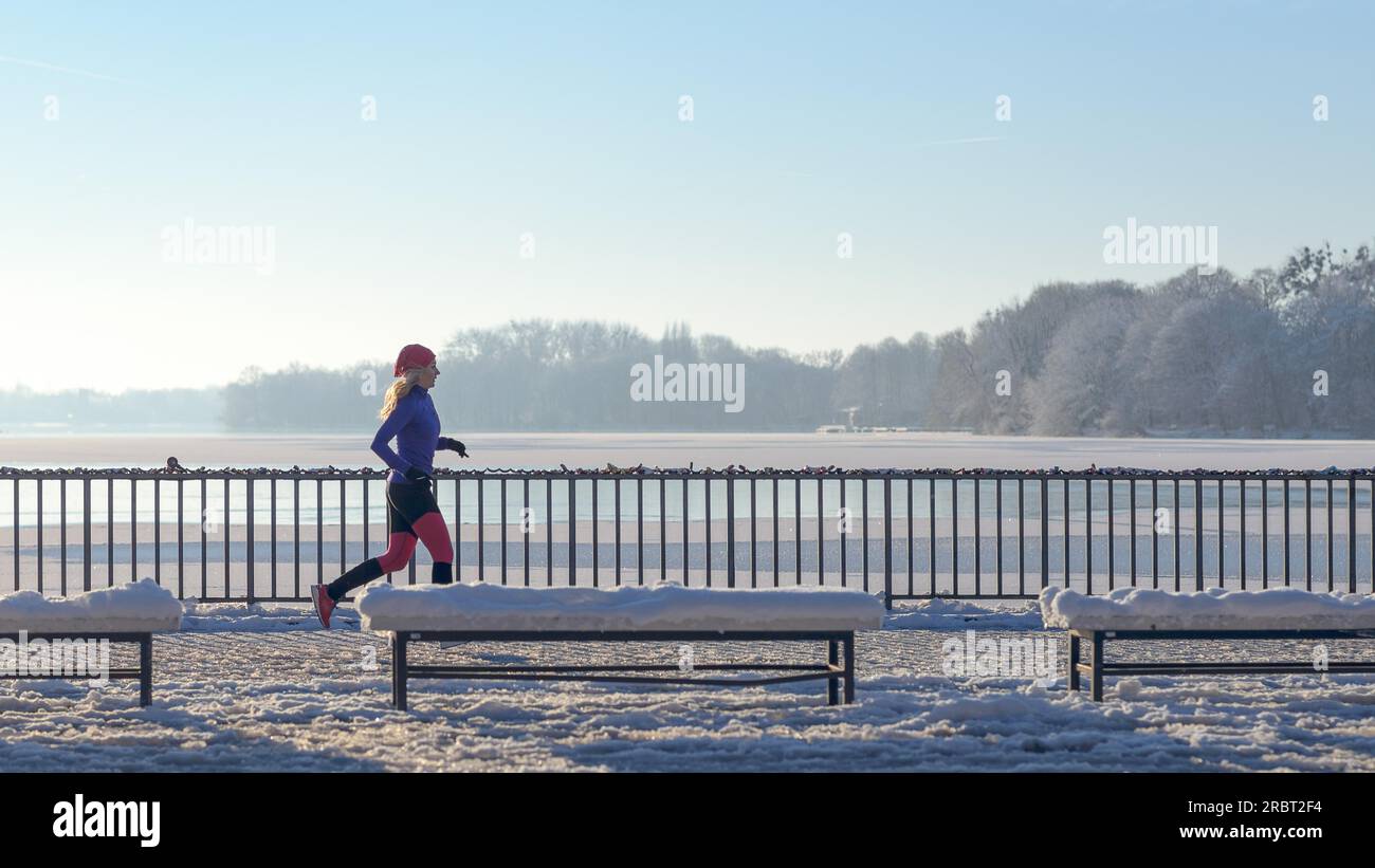 Young woman running in winter snow along a promenade overlooking the ...
