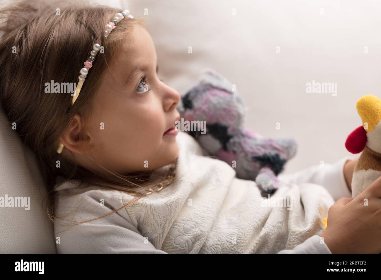 Adorable girl nestled on her couch, playing and caring for her stuffed ...