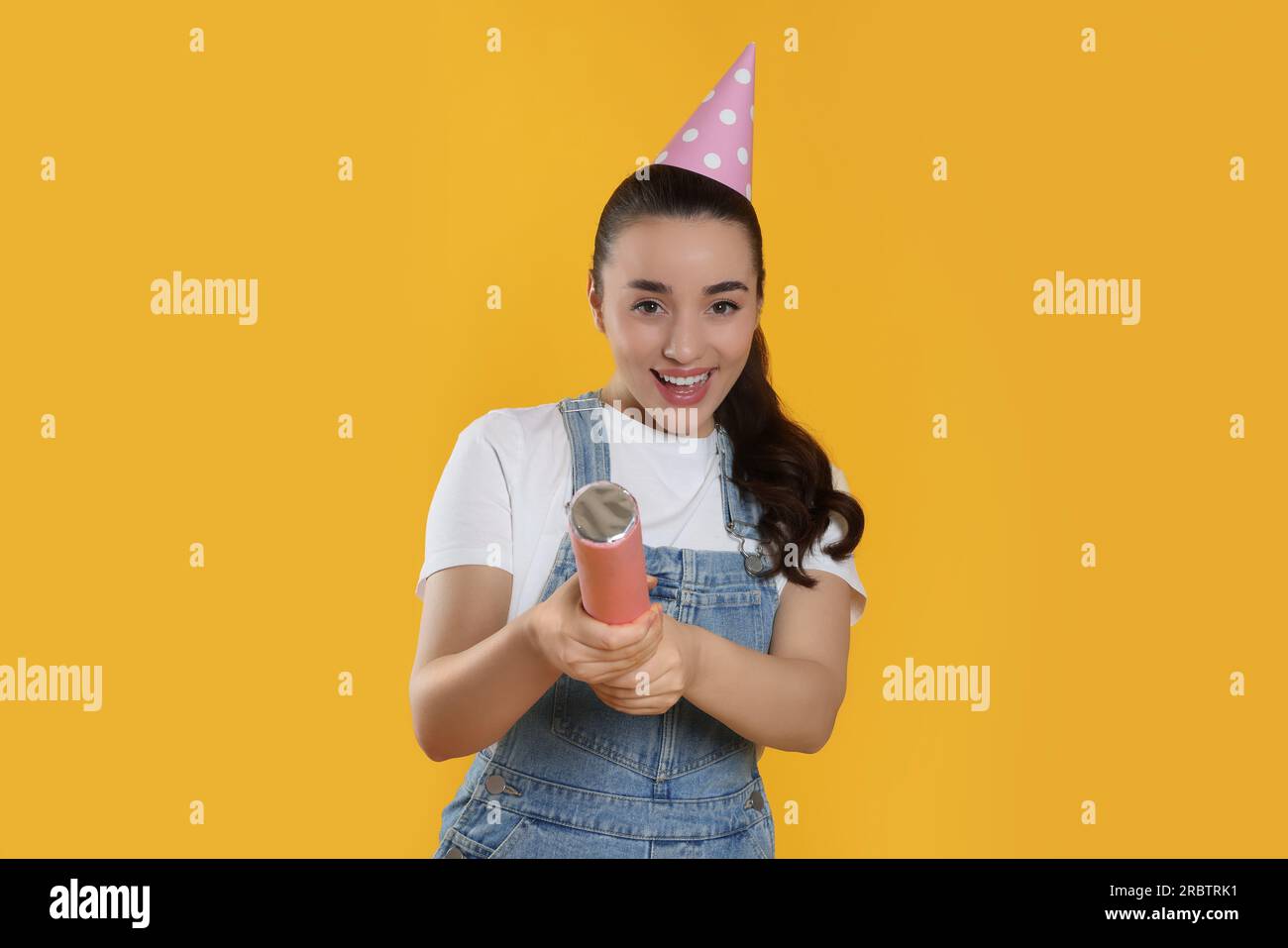 Young woman blowing up party popper on yellow background Stock Photo ...