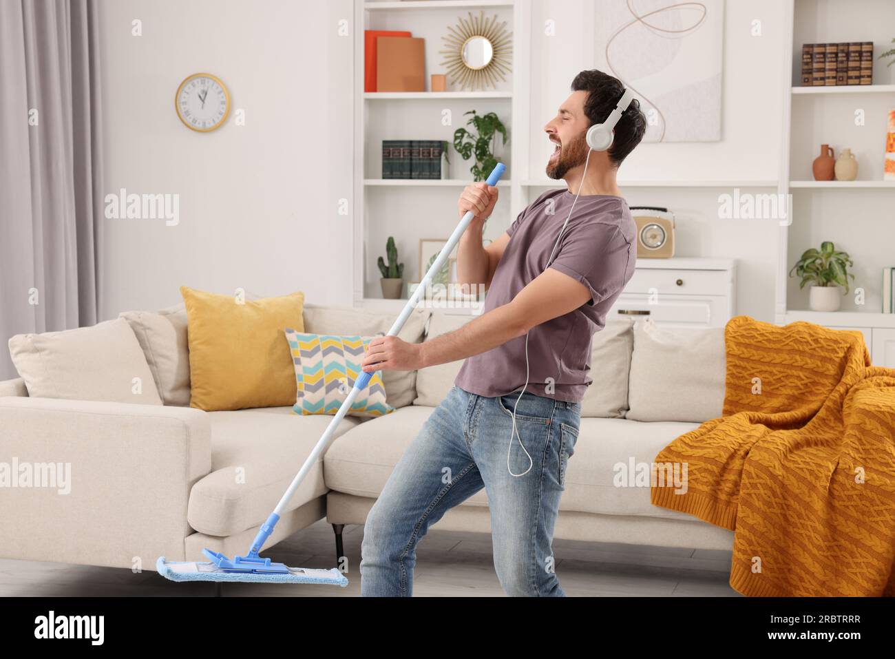Spring cleaning. Man in headphones with mop singing while tidying up ...