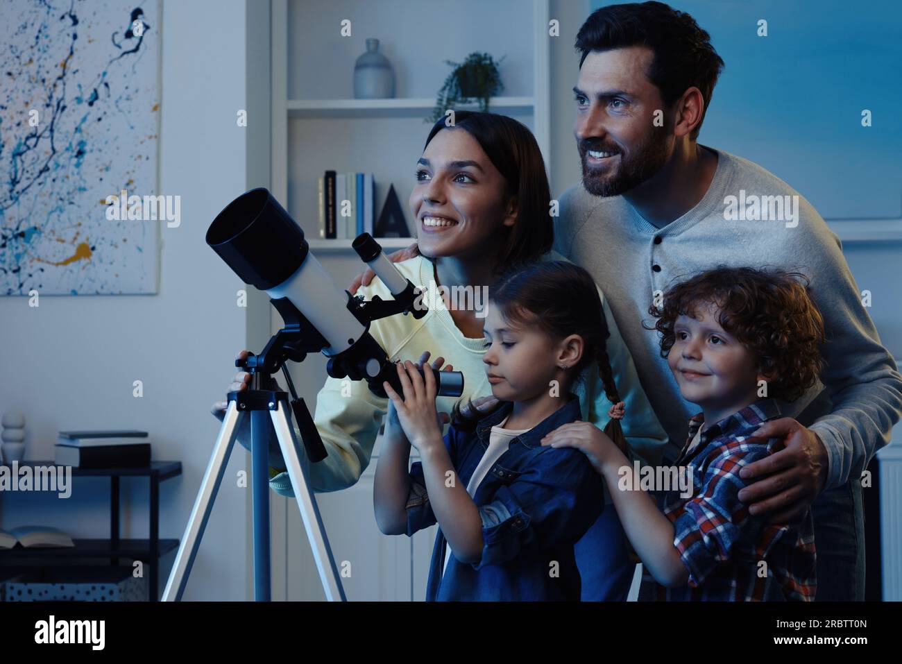Happy family looking at stars through telescope in room Stock Photo - Alamy