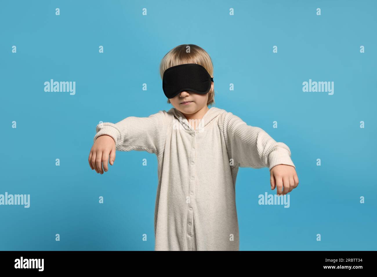 Boy in pajamas and sleep mask sleepwalking on light blue background ...