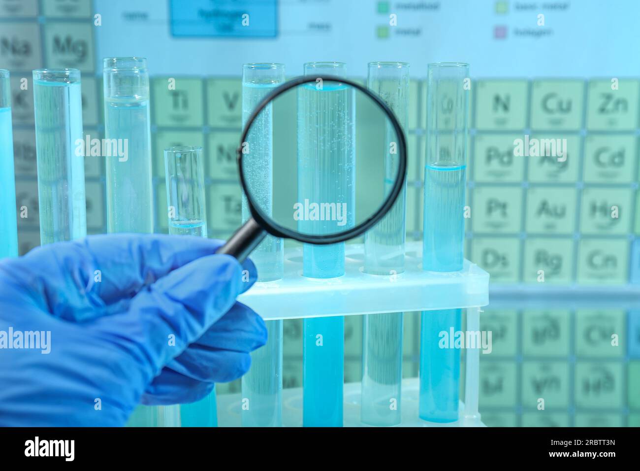 Laboratory assistant looking through magnifying glass on test tubes ...