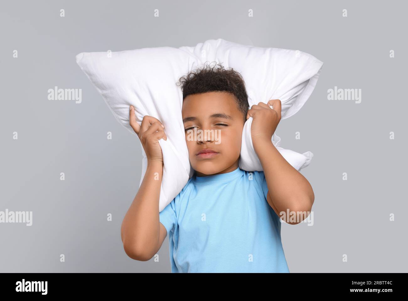 Boy covering his ears with pillow on grey background. Insomnia problem ...