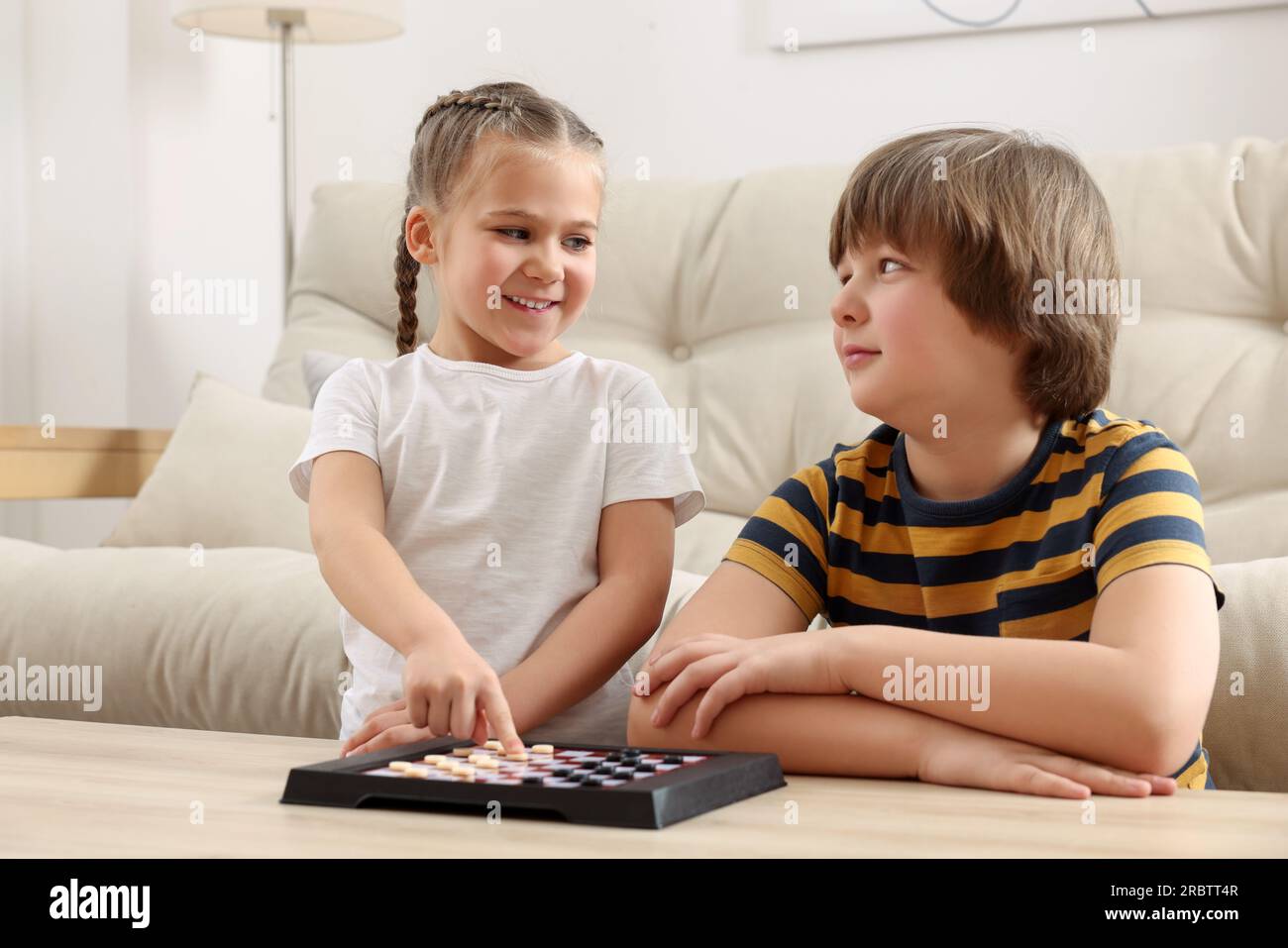 Cute boy playing checkers with little girl at light wooden table in ...