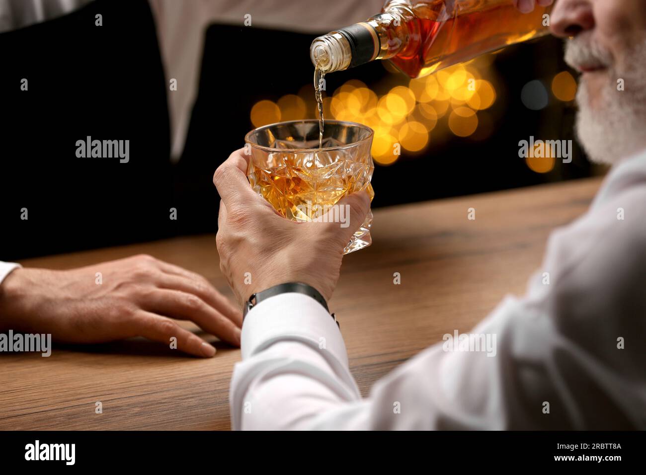 Bartender pouring whiskey in glass for customer at bar counter, closeup ...