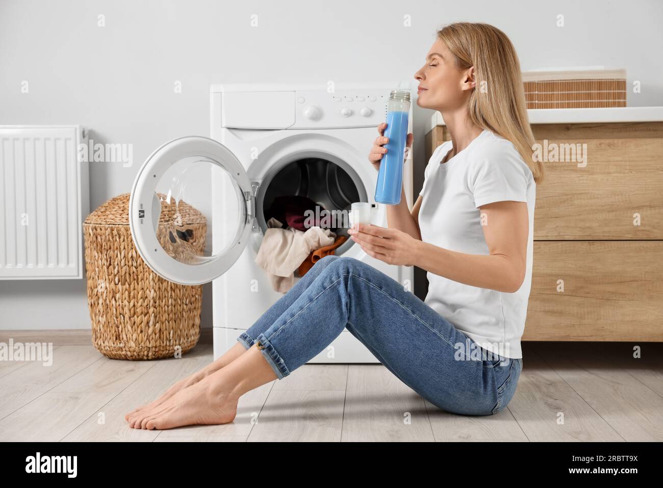 Woman sitting on floor near washing machine and smelling fabric ...
