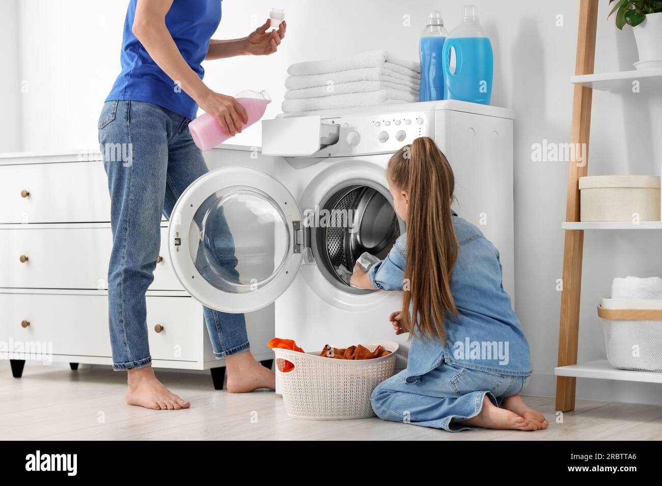 Mother pouring fabric softener and daughter putting dirty clothes into ...