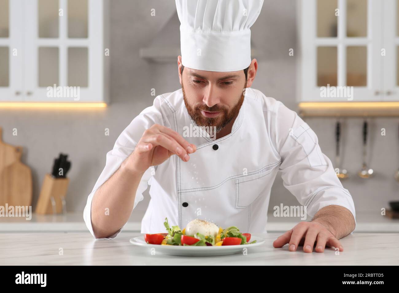 Professional chef salting delicious salad at marble table in kitchen ...