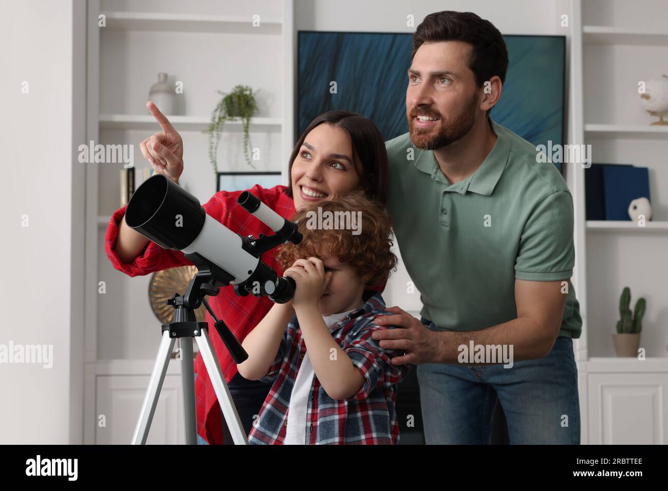 Happy family looking at stars through telescope in room Stock Photo - Alamy