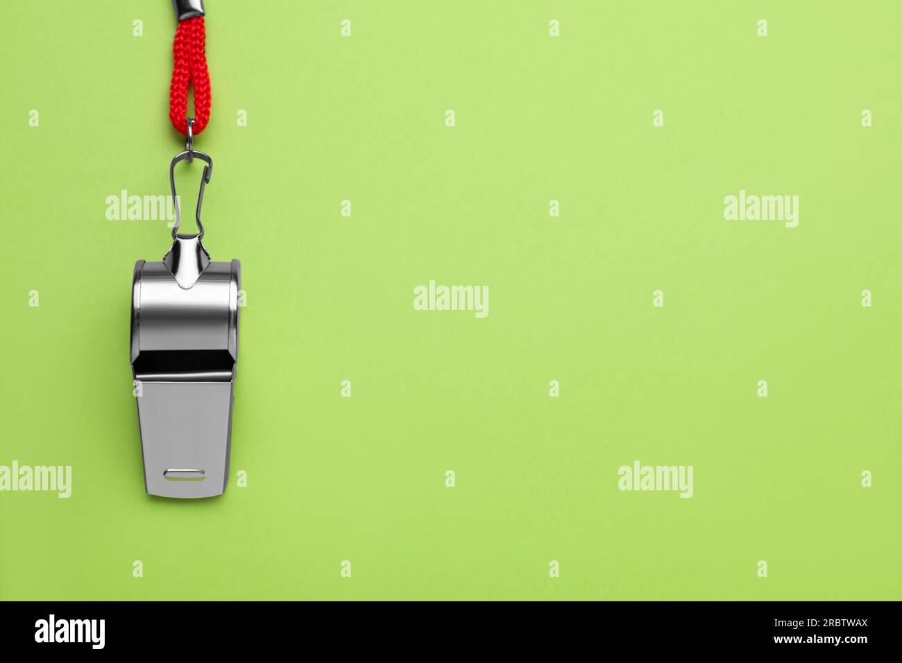 One metal whistle with red cord on light green background, top view ...