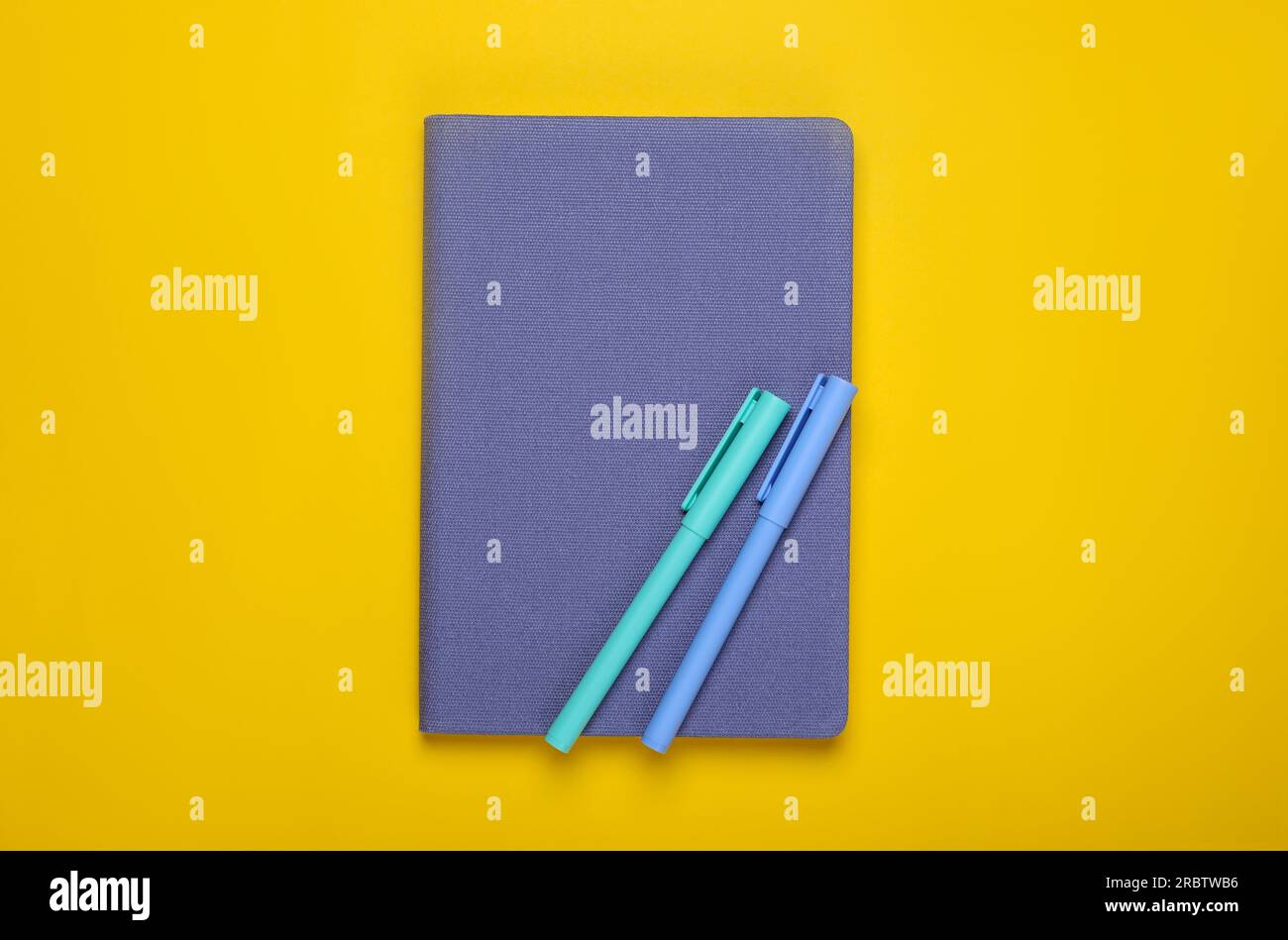 Closed blue notebook and pens on yellow background, top view Stock ...