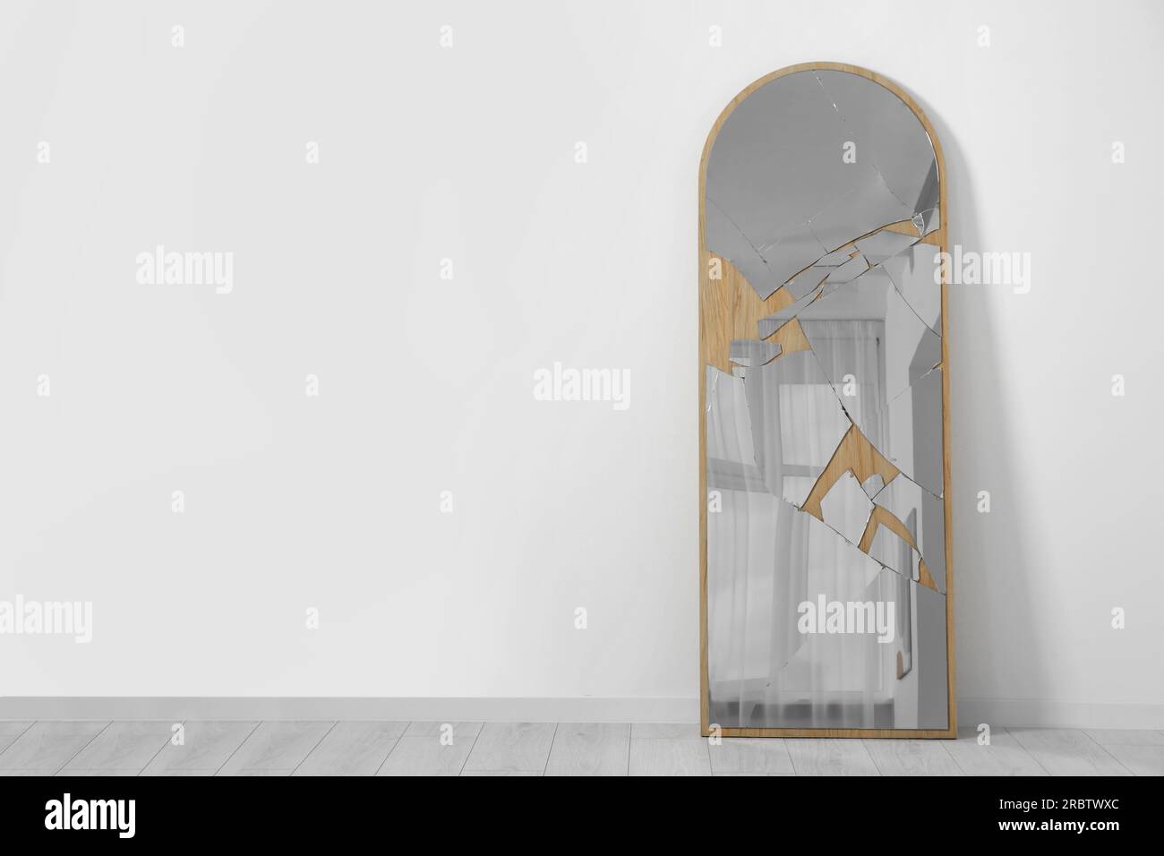 Broken mirror with many cracks near white wall indoors. Space for text ...