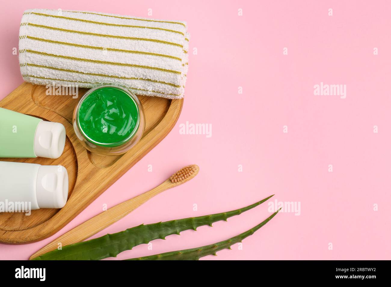 Tubes of toothpaste, fresh aloe, toothbrush and towel on pink ...