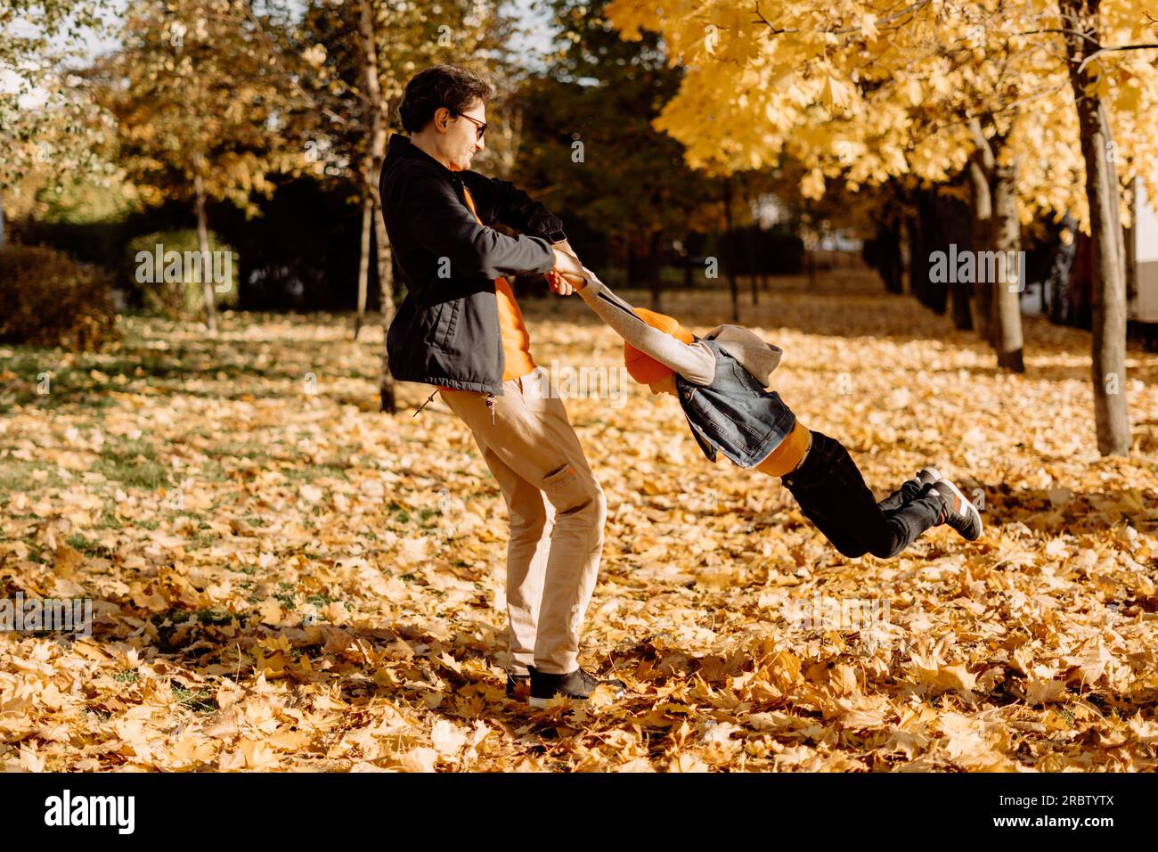 Father and son having fun in autumn park with fallen leaves, throwing ...