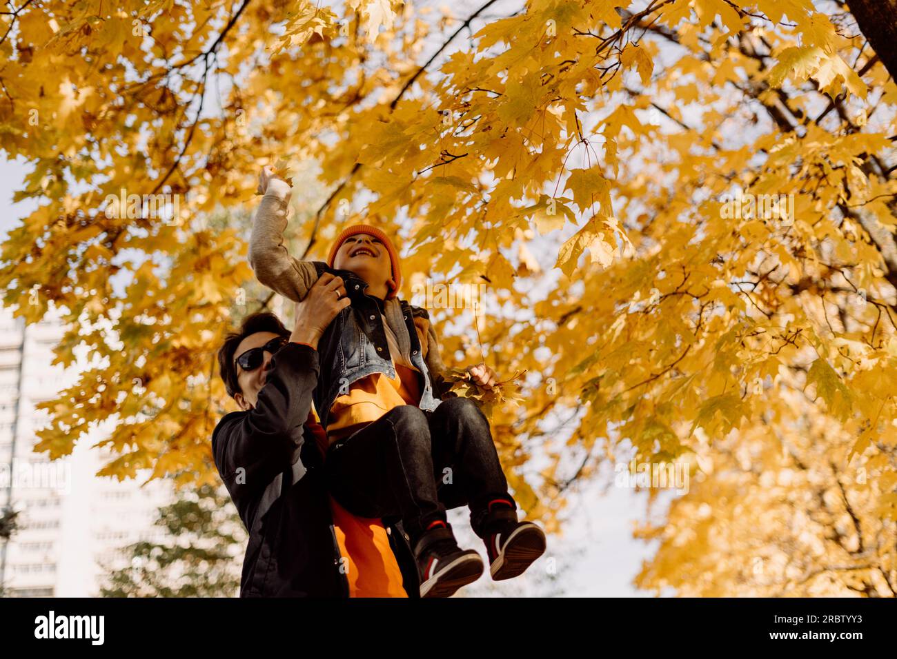 Father and son having fun in autumn park with fallen leaves, throwing ...